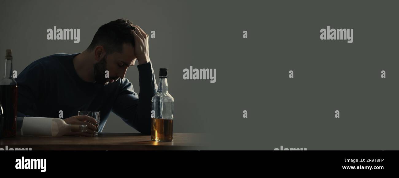 Suffering from hangover. Man with alcoholic drink at table against grey ...