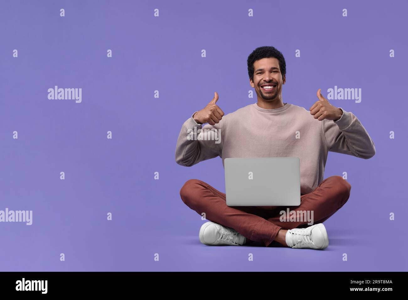 Smiling man with laptop showing thumbs up on purple background. Space ...