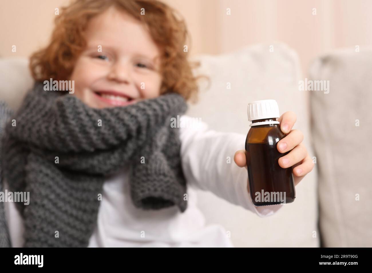 Cute boy holding bottle with cough syrup on sofa, focus on hand ...