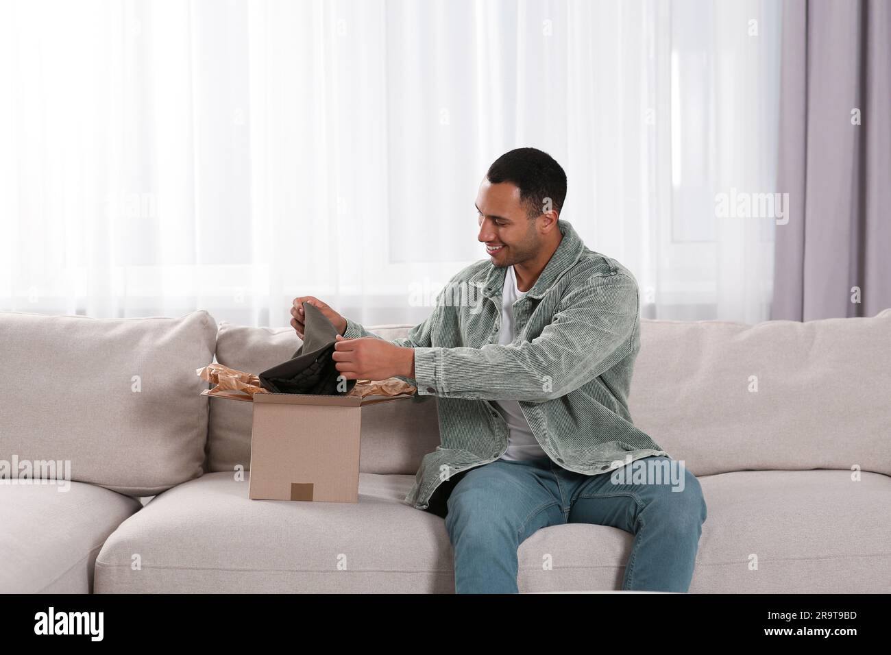 Happy young man opening parcel at home. Internet shopping Stock Photo ...