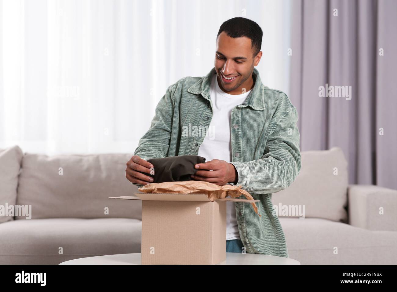 Happy young man opening parcel at home. Internet shopping Stock Photo ...