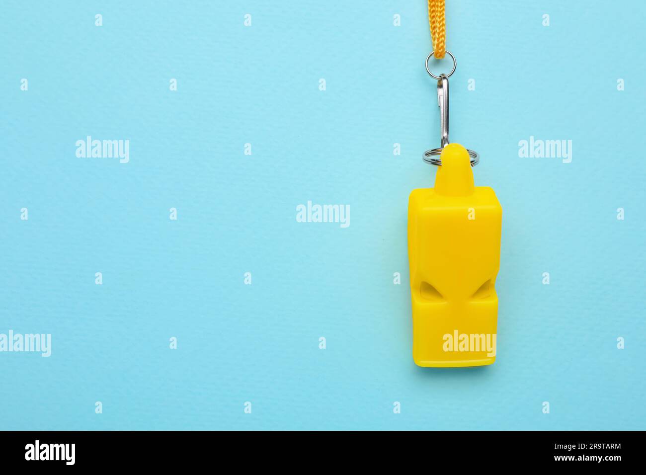 One yellow whistle with cord on light blue background, top view. Space ...