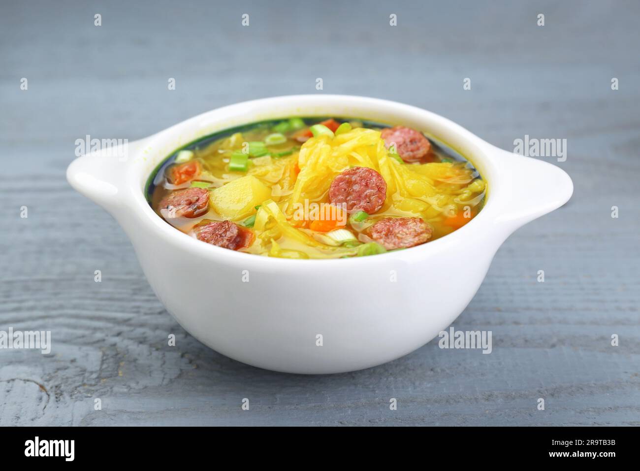 Delicious sauerkraut soup with smoked sausages and green onion on grey ...