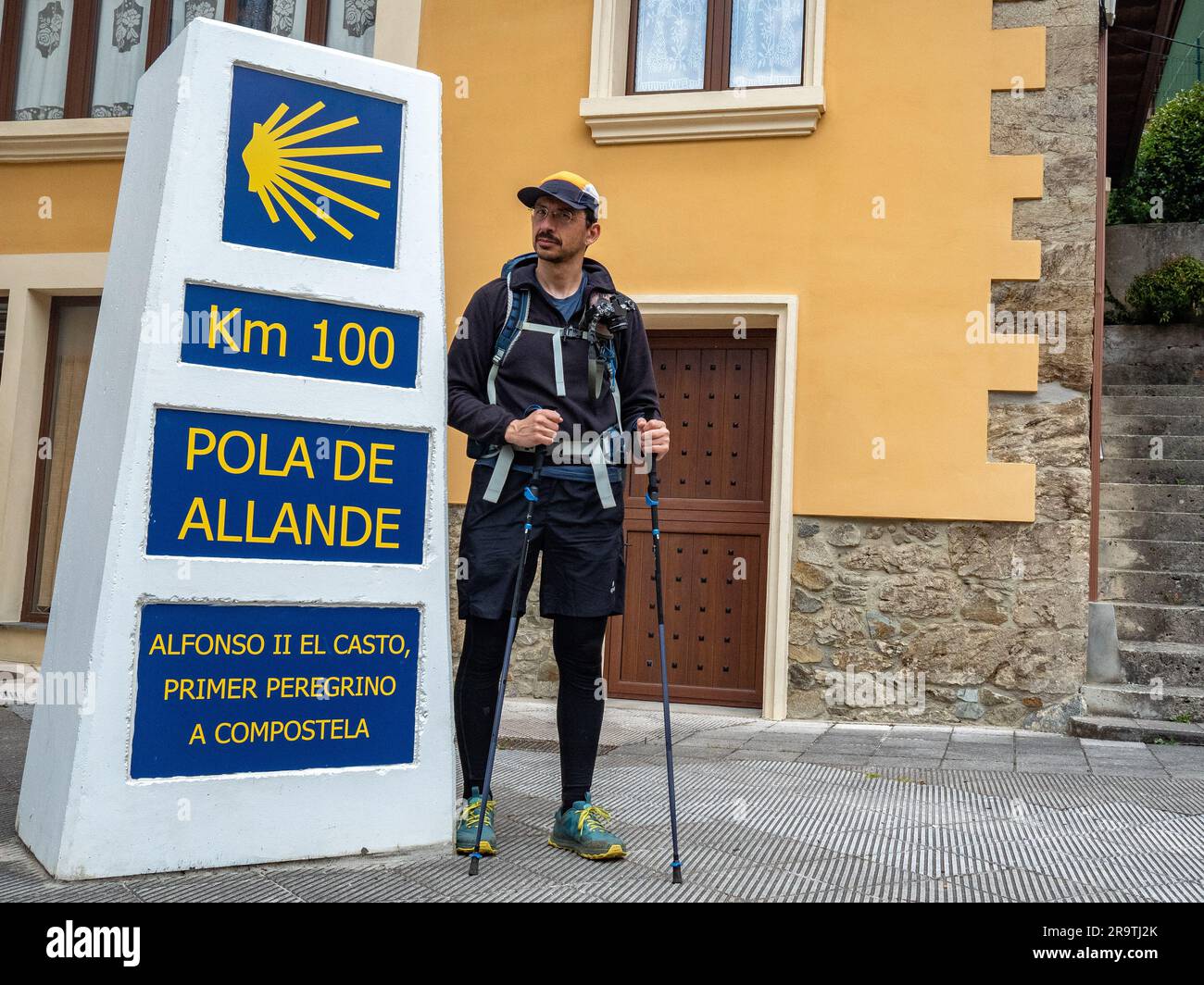A pilgrim is seen posing next to a huge stone mark that is pointing to ...