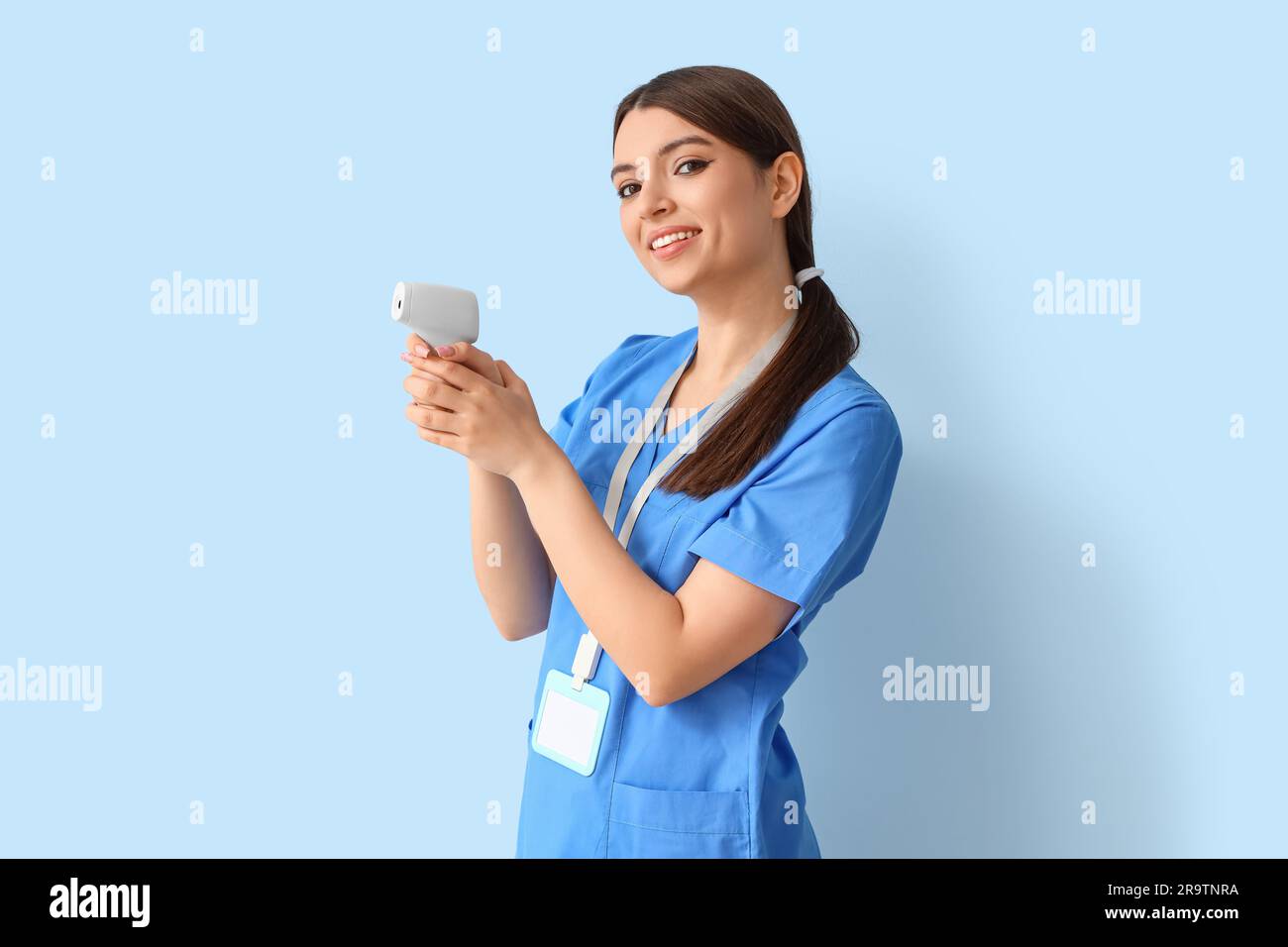 Female medical intern with infrared thermometer on blue background ...