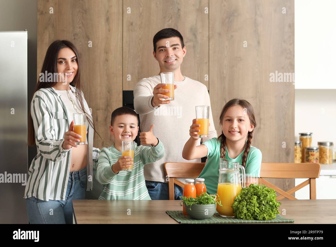 Happy parents with their little children drinking orange juice in ...