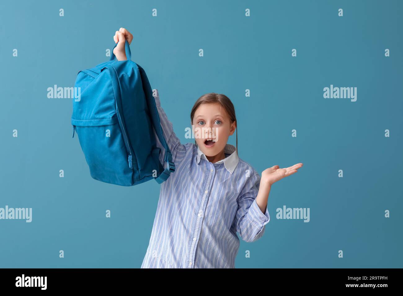 Shocked little schoolgirl with backpack on blue background Stock Photo ...
