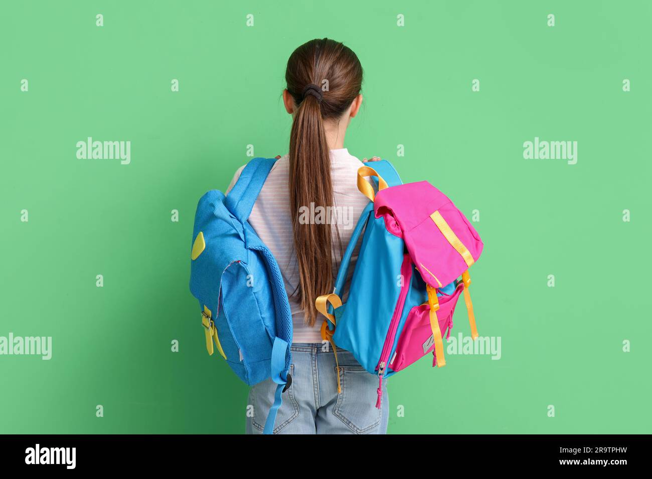 Little girl with backpacks on green background, back view Stock Photo ...
