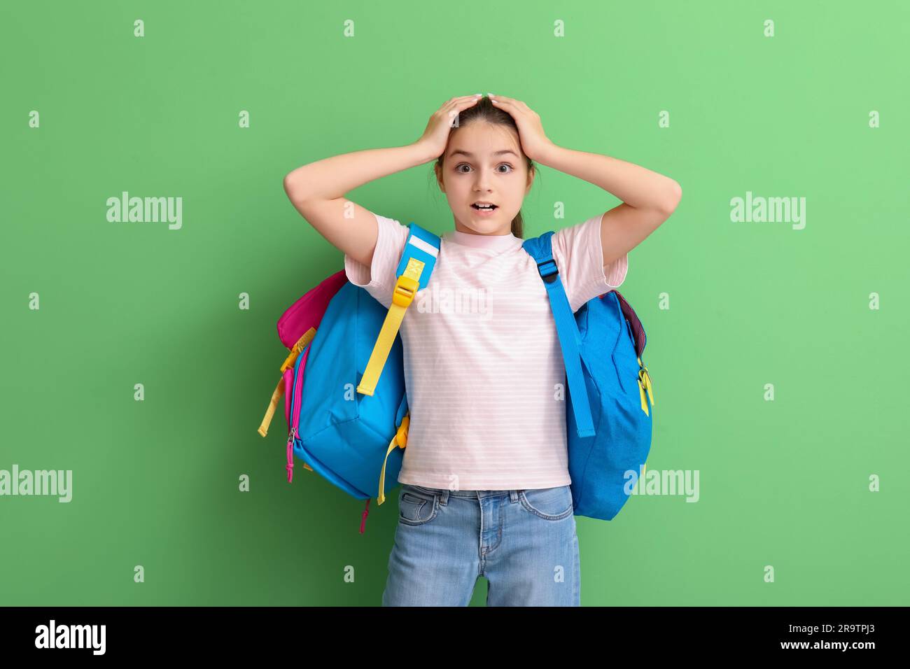 Shocked little girl with backpacks on green background Stock Photo - Alamy