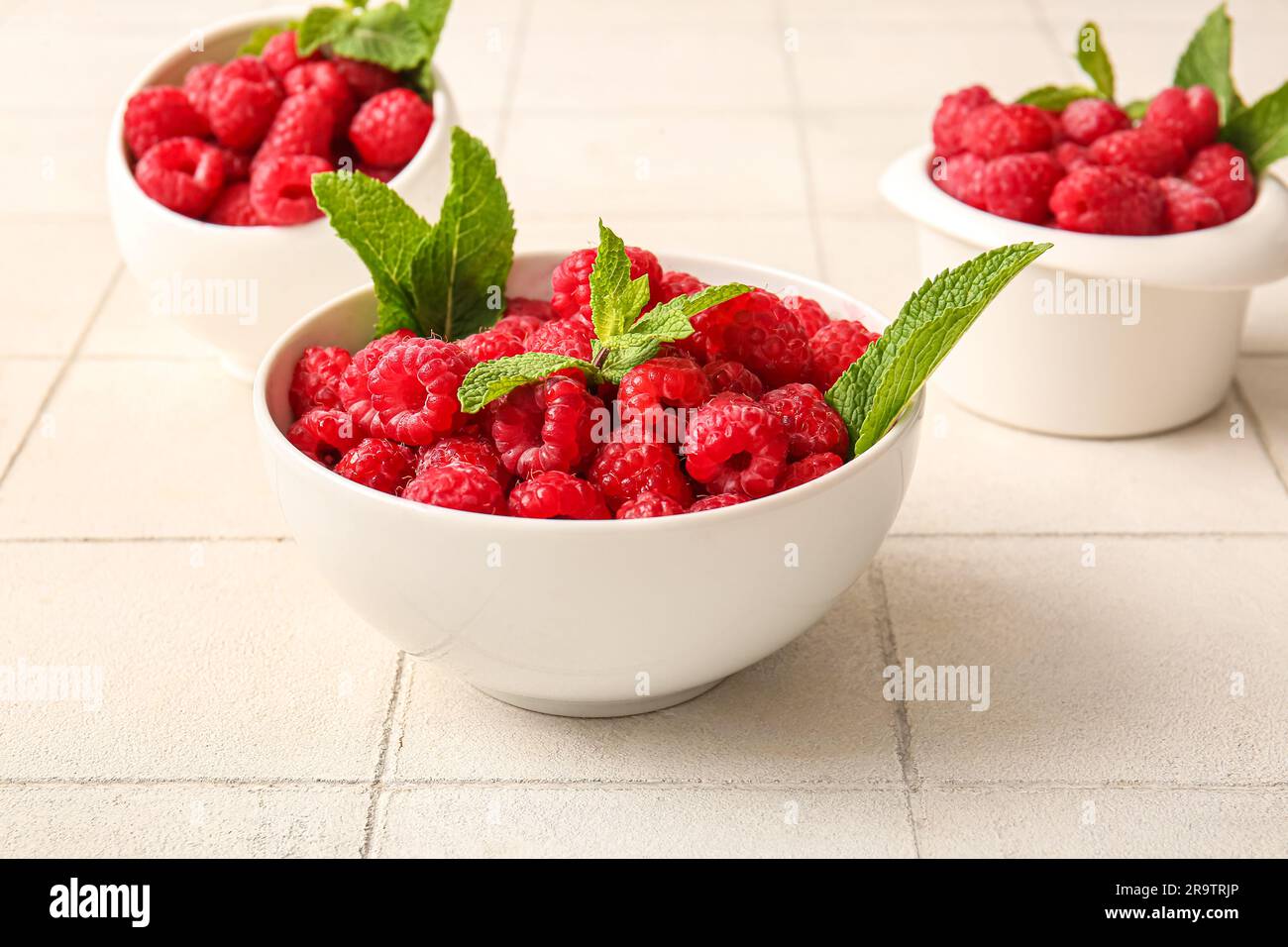 Bowls with fresh raspberries and mint on white tile background Stock ...