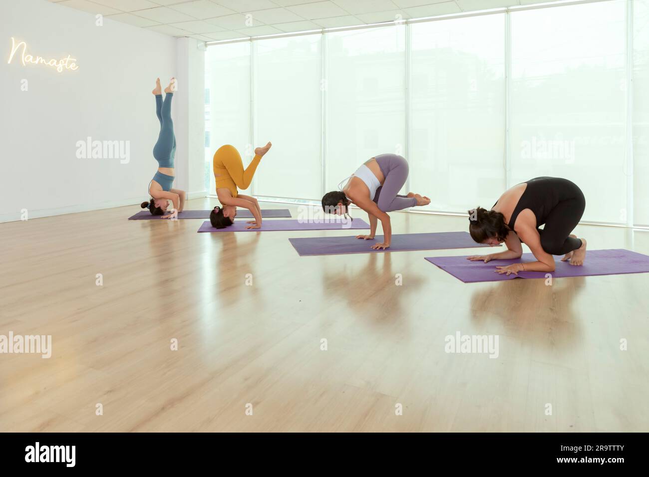 Four women doing the progression of a yoga pose indoors in a studio ...
