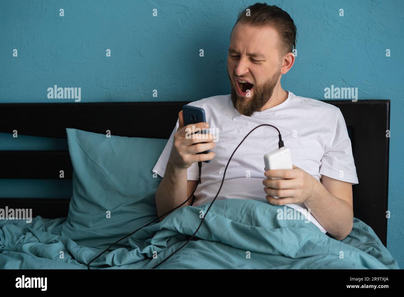 Handsome man connects his smartphone to a power bank while lying on the ...