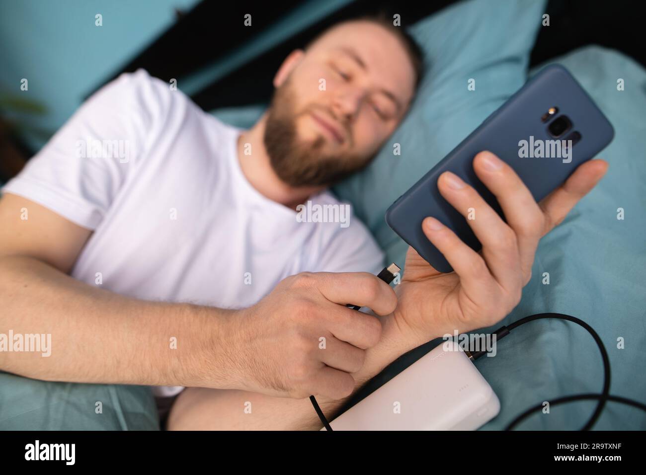 Serious millennial man using mobile phone in bed connect it to a ...