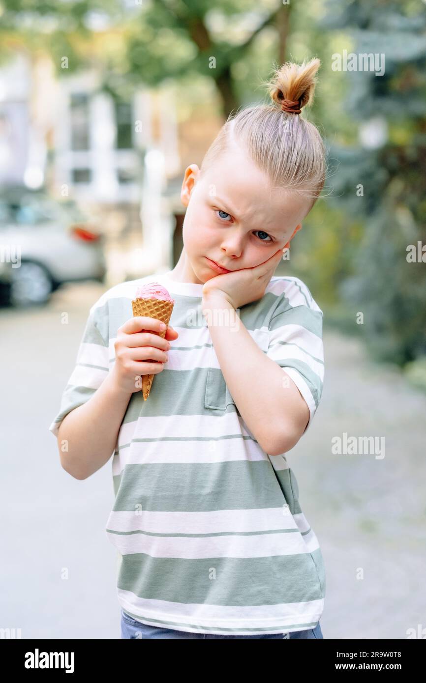 Sad child clutched his cheek with his hand and held an ice cream cone ...