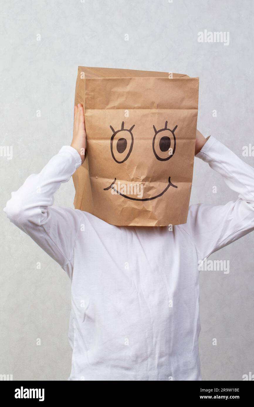 The boy has a cardboard box above his head with a funny smiley face ...