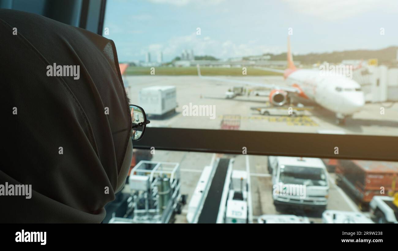 Asian woman wearing hijab smiling looking at airplane while waiting for ...