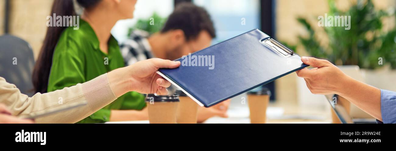 Male coworker giving a folder with documents to his colleague while ...