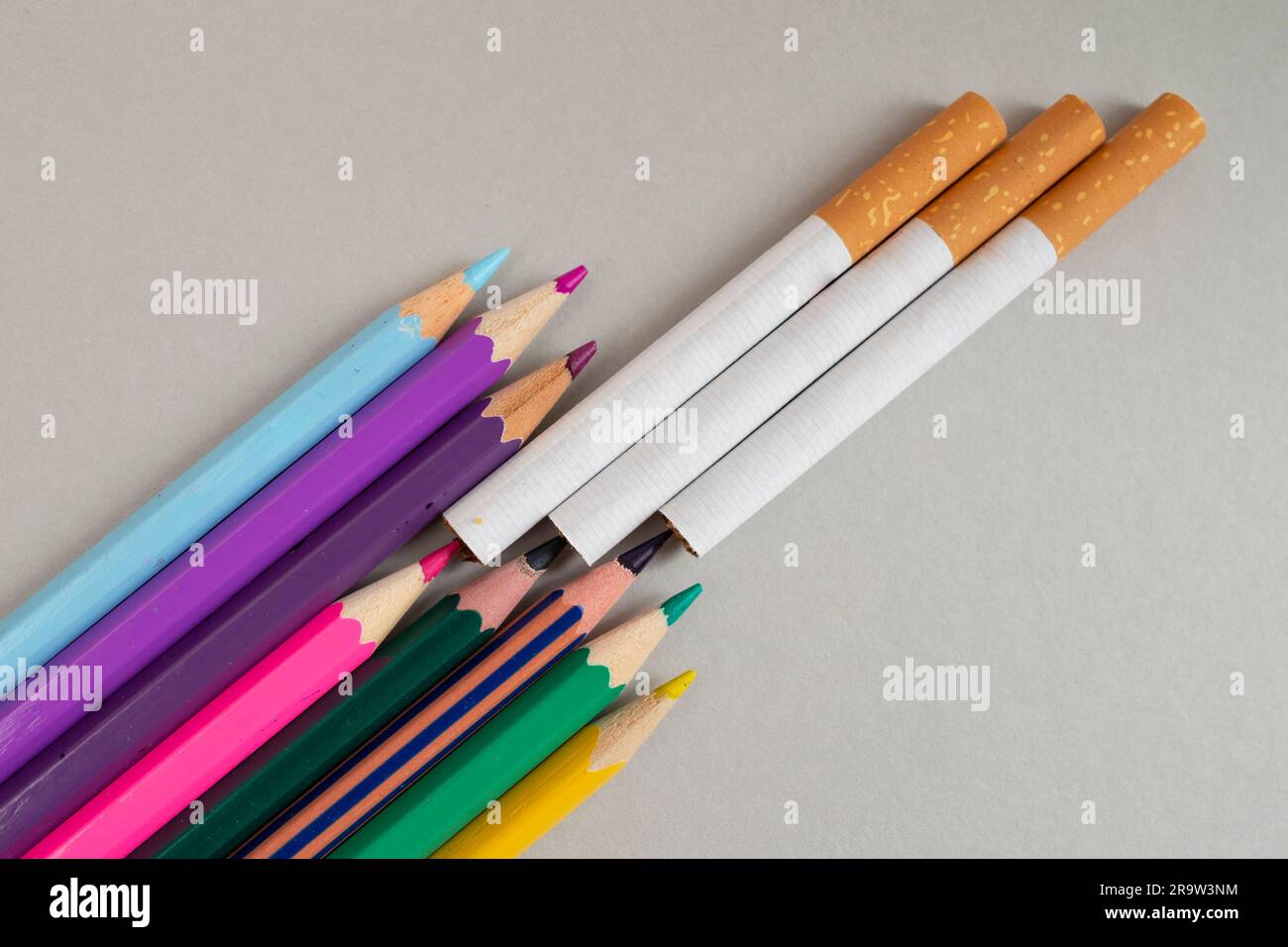 cigarettes between colored crayons on gray paper backdrop, soft focus ...