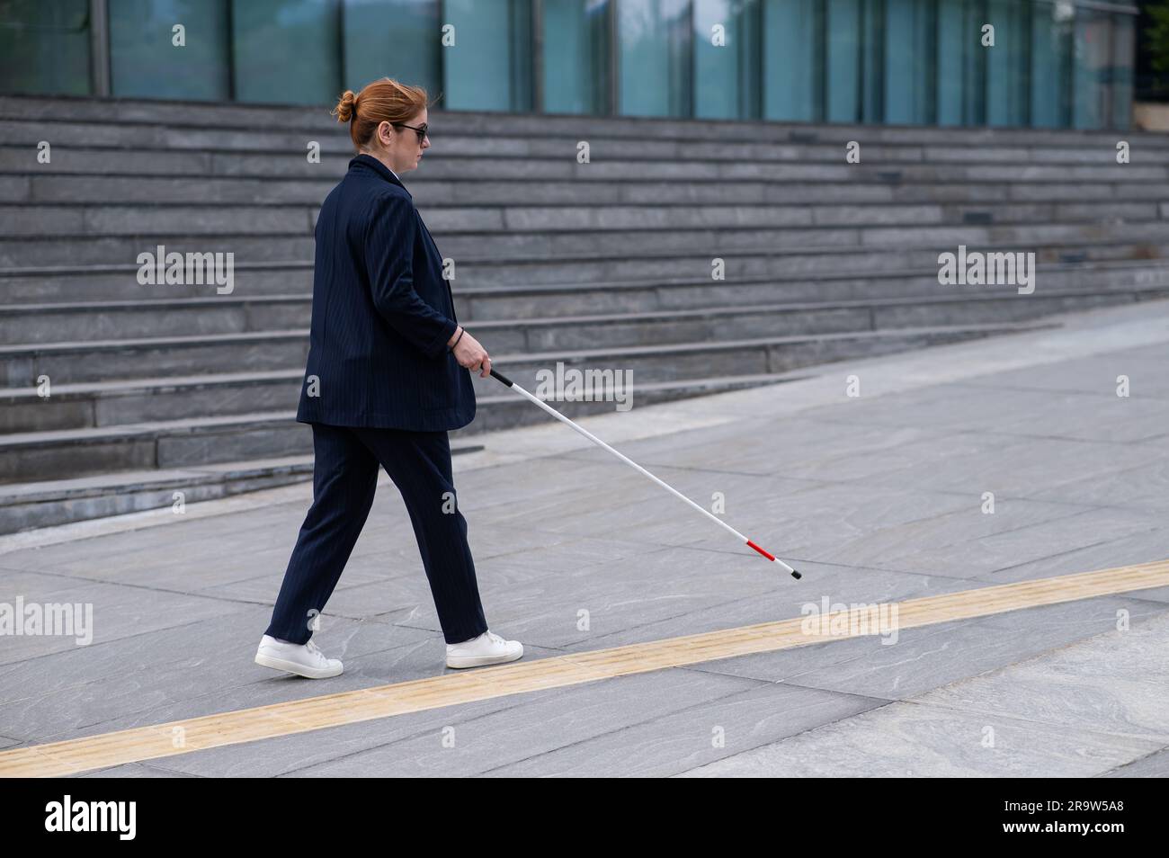 Blind businesswoman walking along tactile tiles with a cane Stock Photo ...