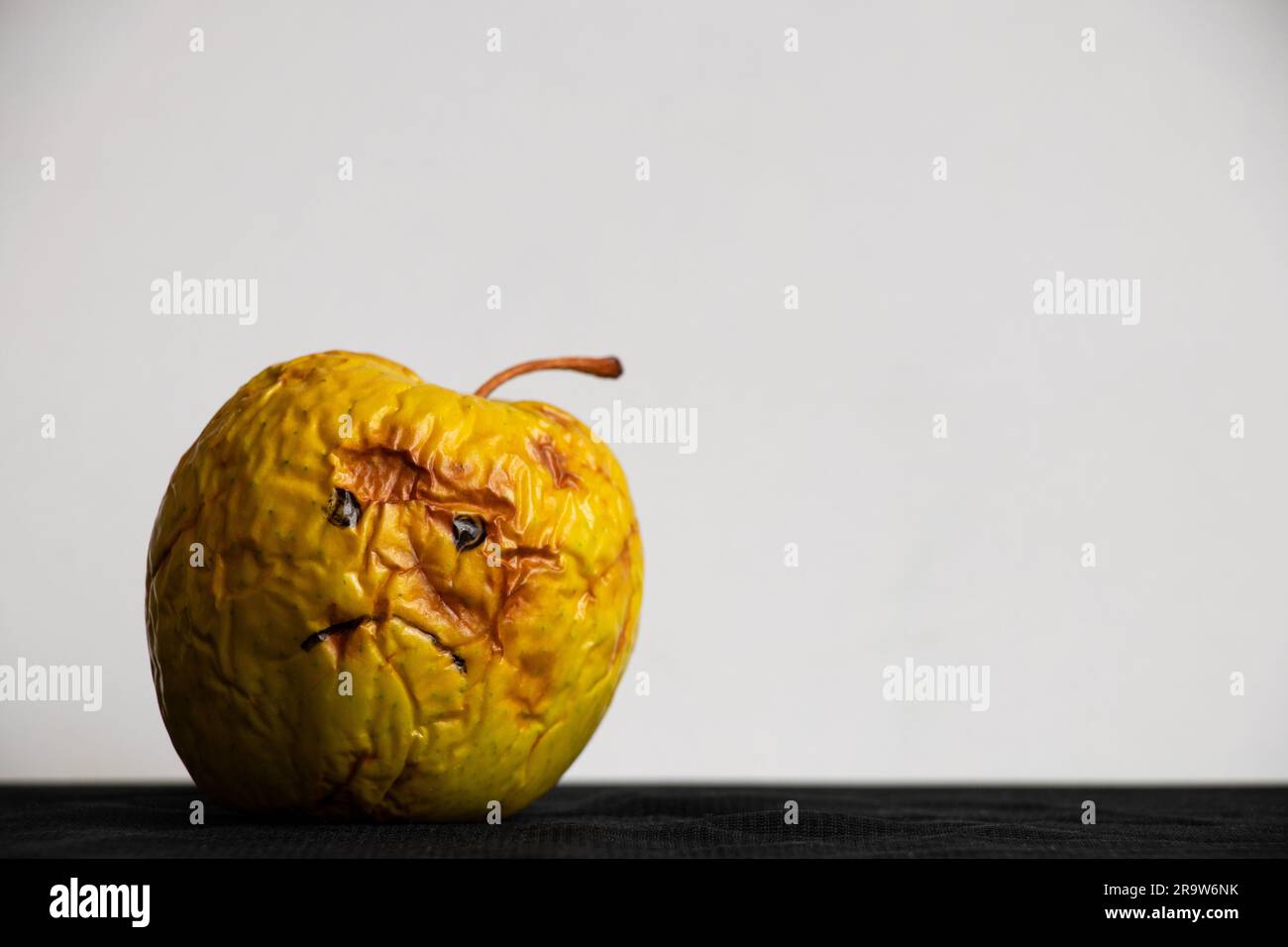 A rotten and sluggish apple with a sad painted smile on a white ...