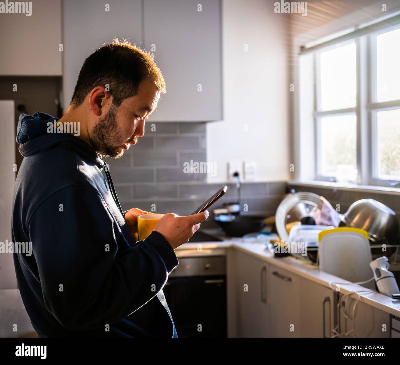 Young man reading smartphone and drinking coffee at home. Pile of ...