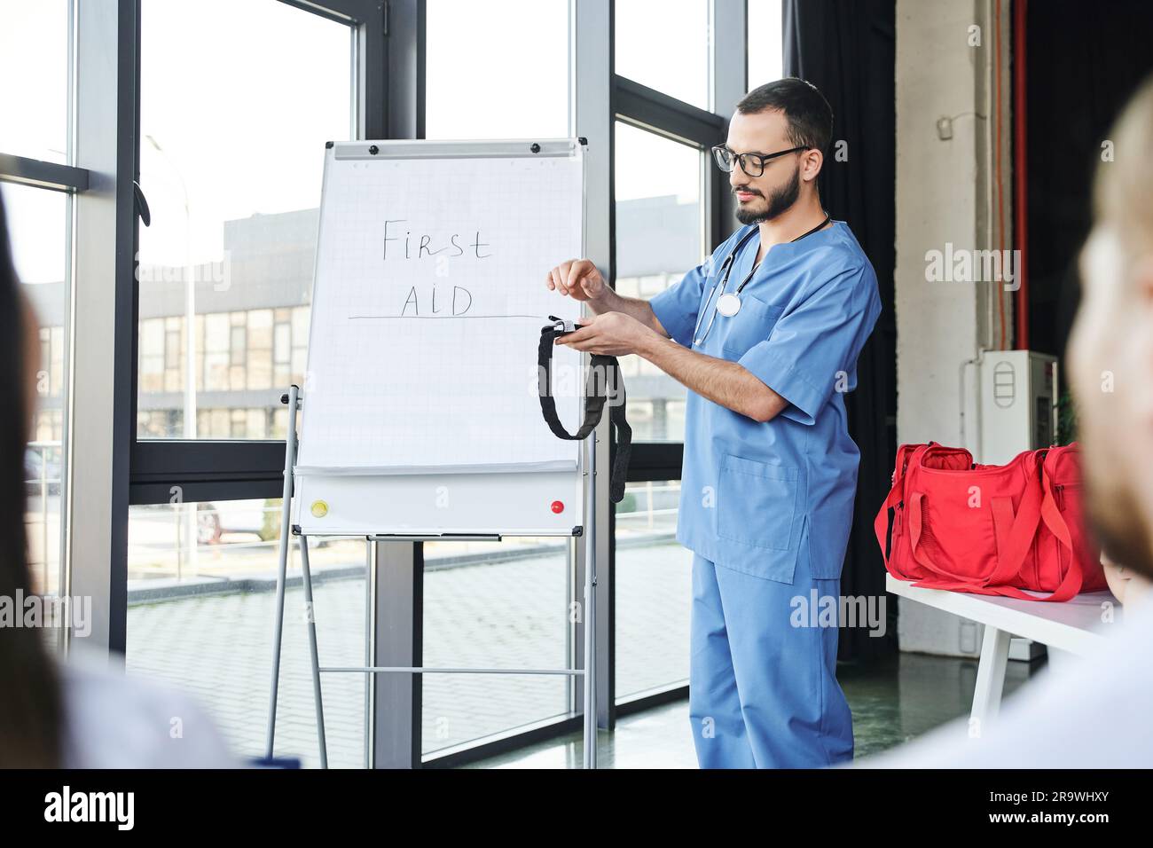paramedic in eyeglasses and blue uniform standing at flip chart with ...