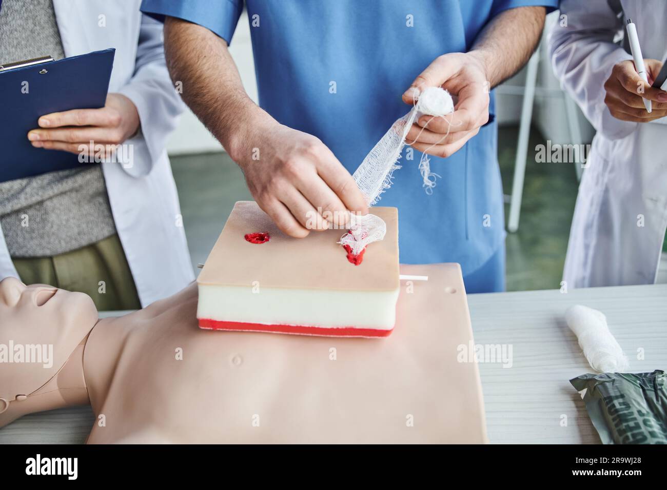 cropped view of medical instructor tamponing wound on simulator with bandage near CPR manikin ...