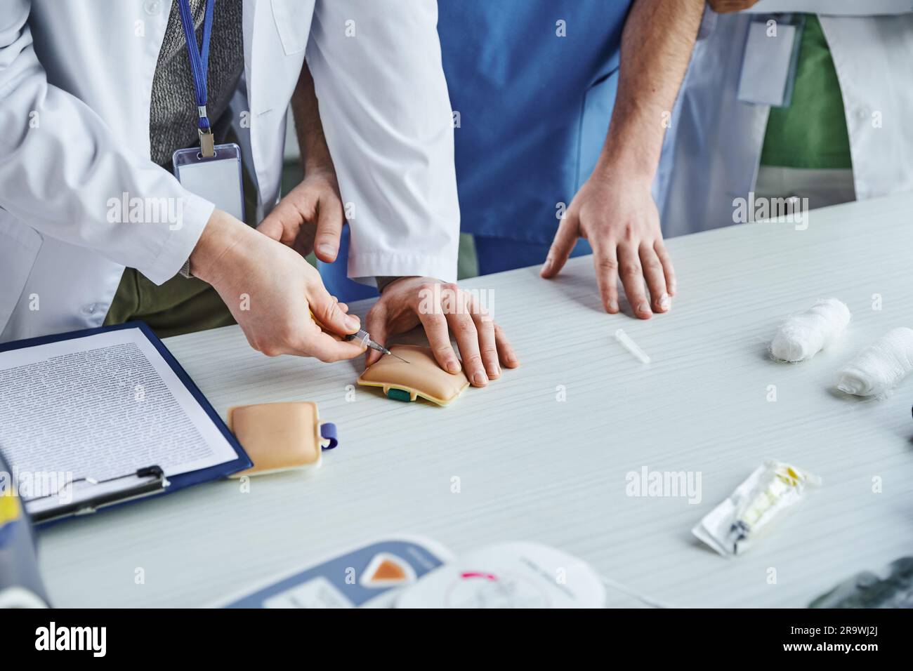 partial view of student in white coat doing injection in training pad near clipboard, bandages ...