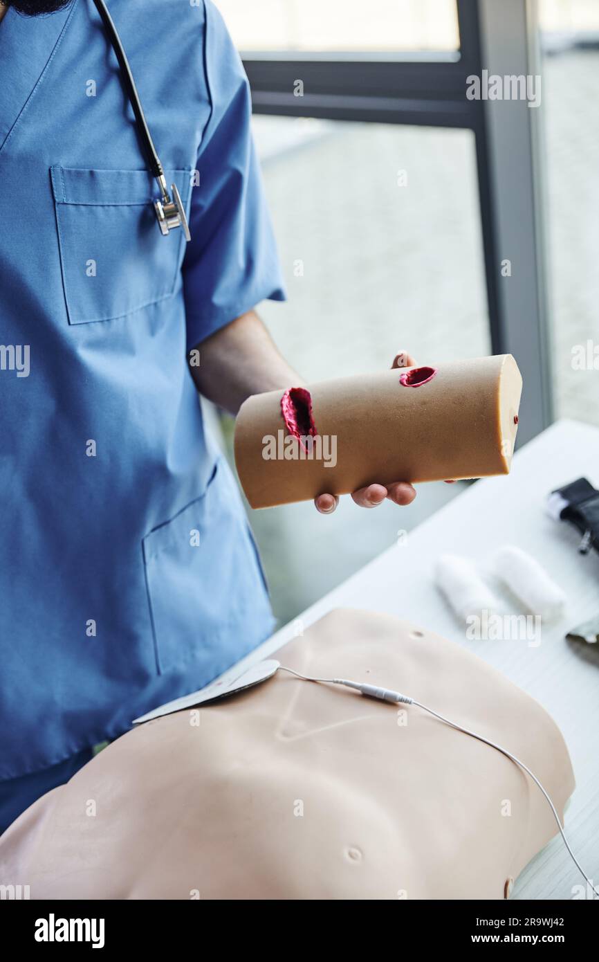cropped view of professional paramedic in blue uniform holding wound care simulator near CPR ...