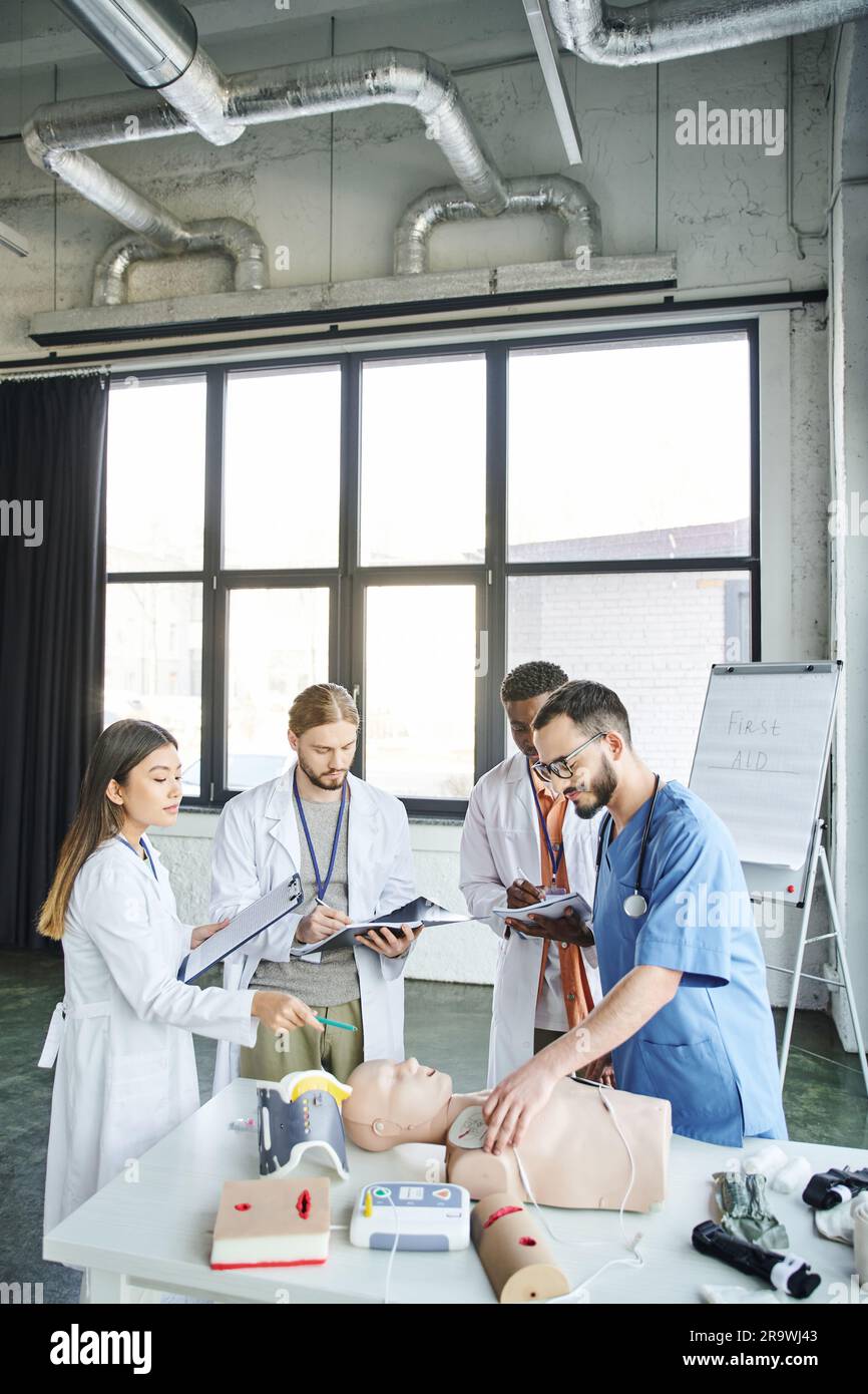 young asian woman pointing with pen at CPR manikin with defibrillator near medical instructor ...