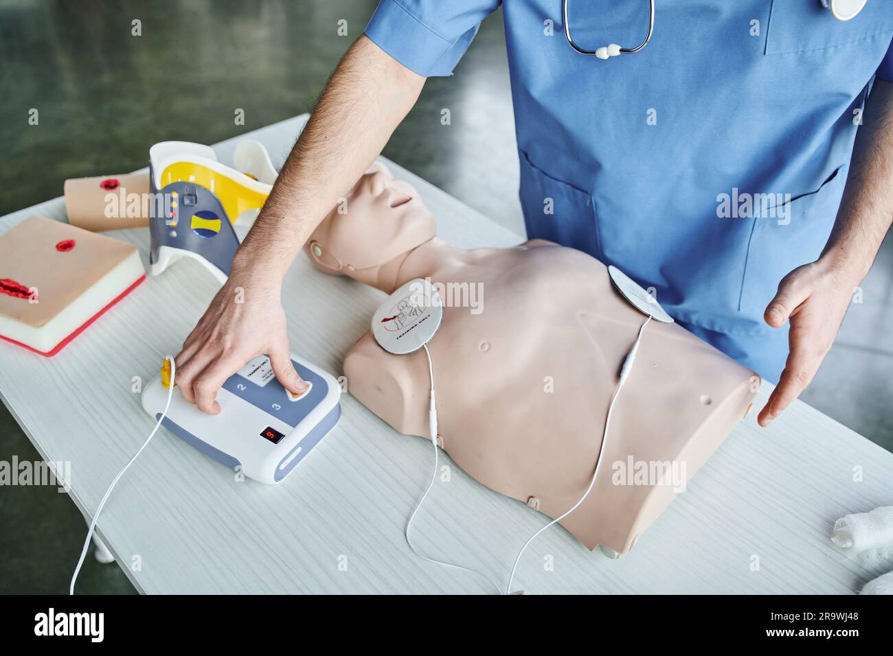 partial view of medical instructor operating automated defibrillator near CPR manikin, wound ...