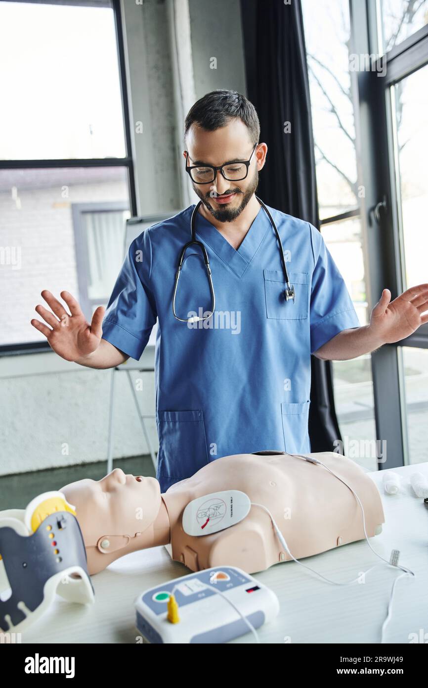 smiling bearded paramedic in blue uniform and eyeglasses gesturing near ...