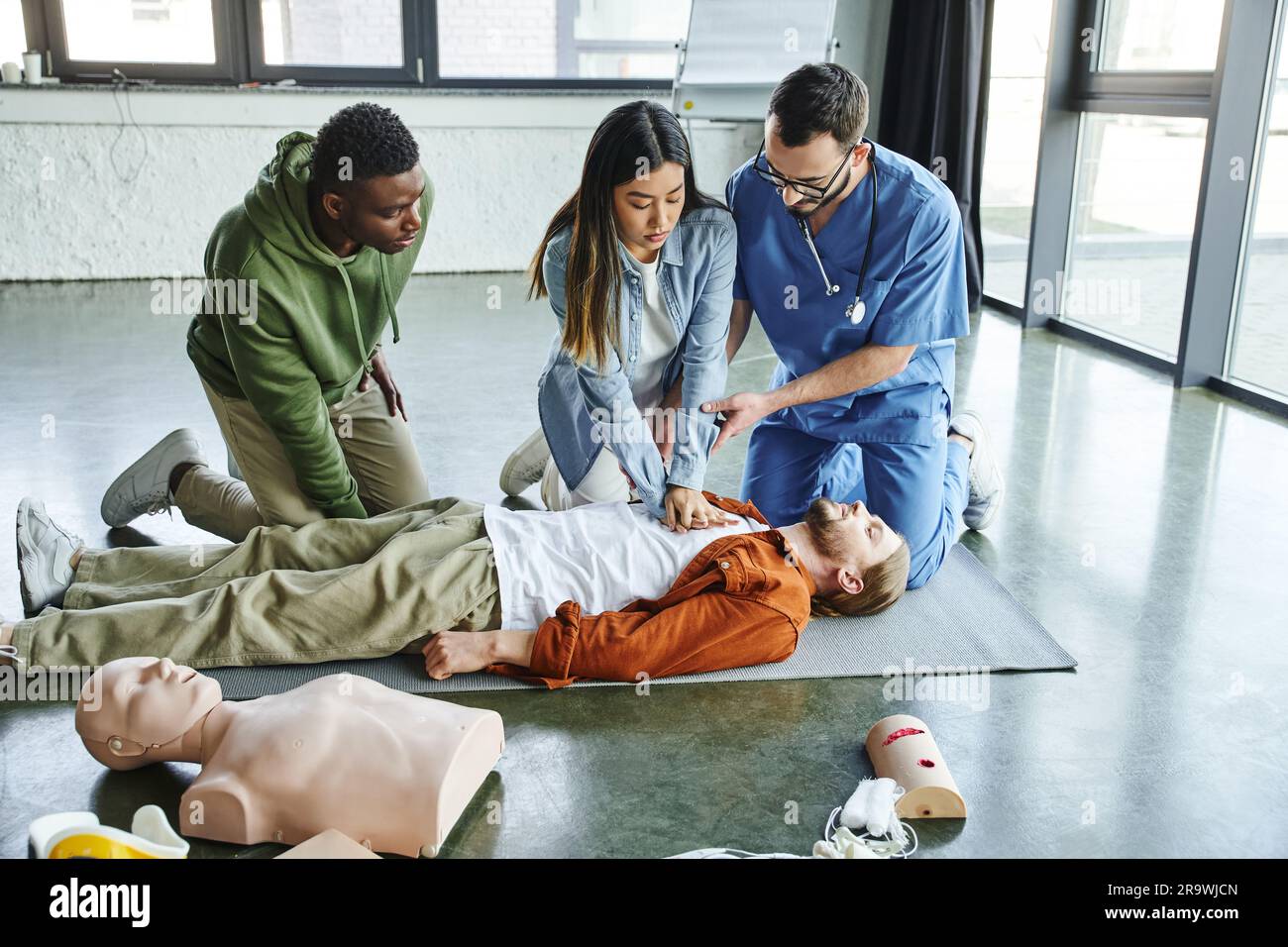 young asian woman doing chest compressions on man near medical instructor, CPR manikin and ...
