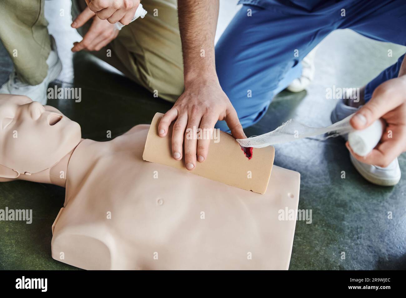 high angle view of medical instructor tamponing wound on simulator with bandage near CPR manikin ...