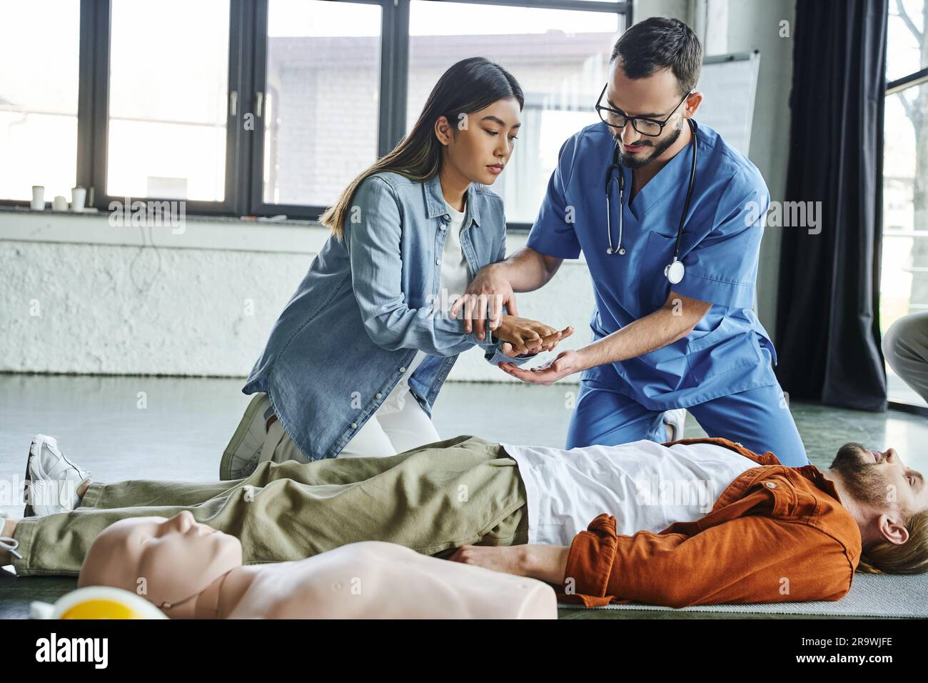 medical instructor showing hands position for cardiopulmonary resuscitation to young asian woman ...