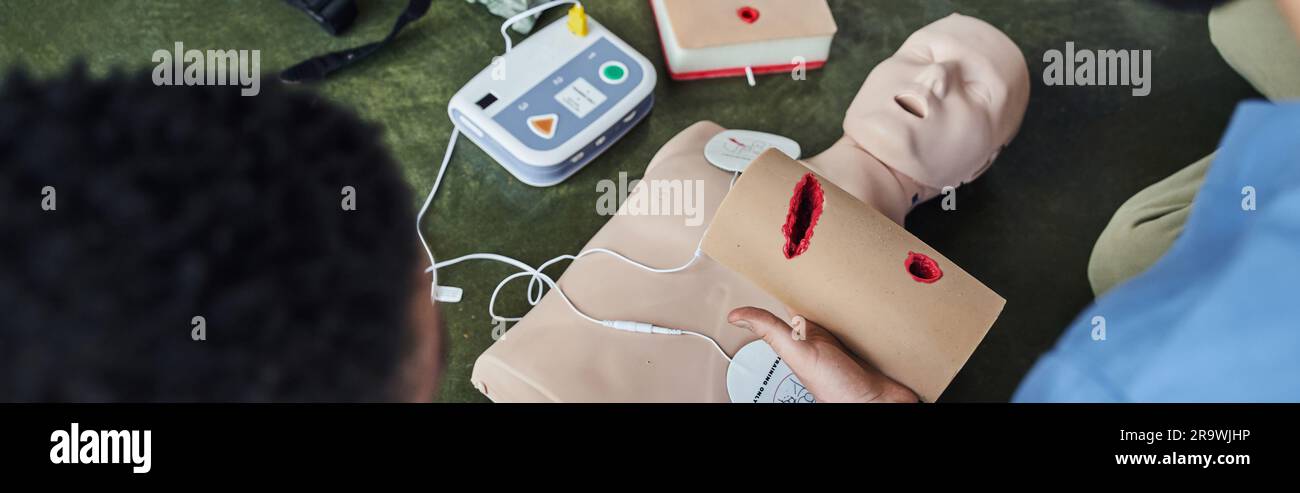 top view of medical instructor holding wound care simulator above CPR manikin and automated ...