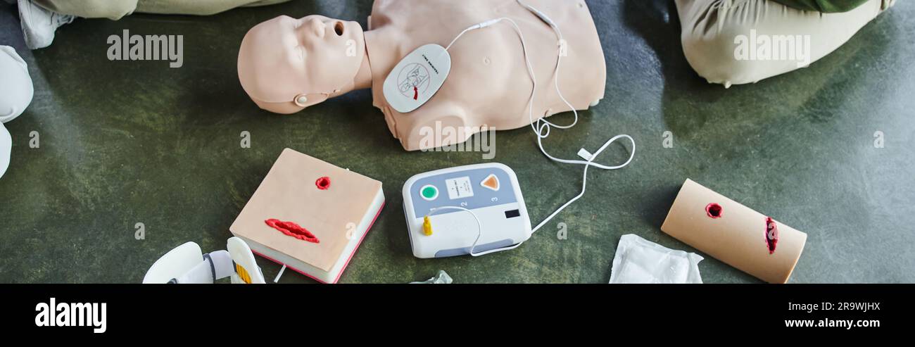 top view of CPR manikin, automated external defibrillator and wound care simulators near cropped ...