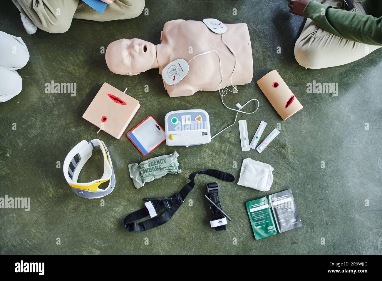 first aid seminar, cropped view of young people near CPR manikin, defibrillator, wound care ...