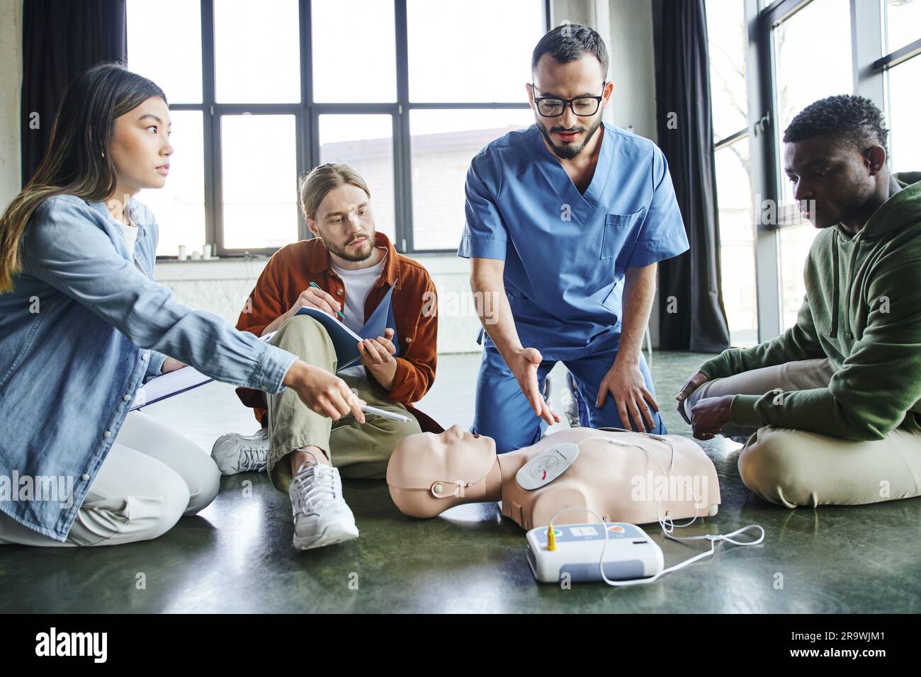 young asian woman and medical instructor pointing at CPR manikin with defibrillator near ...