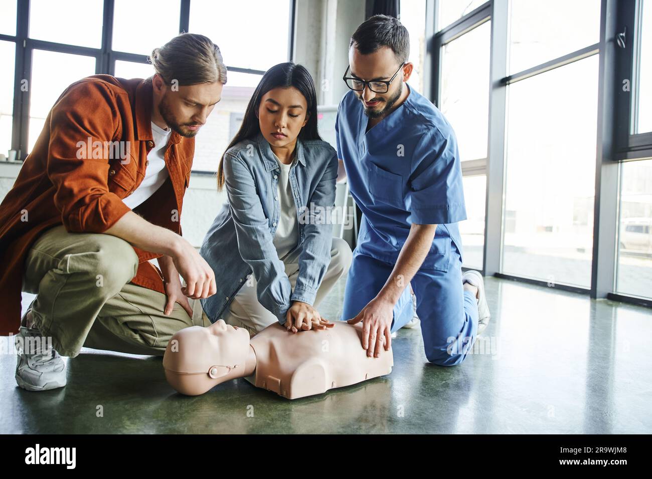 asian woman practicing chest compressions on CPR manikin near young man and medical instructor ...