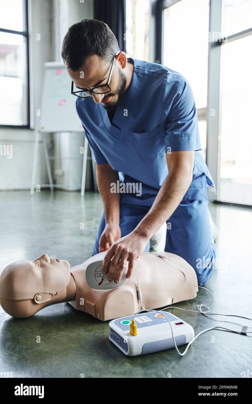 first aid training seminar, young medical instructor in uniform and eyeglasses applying ...