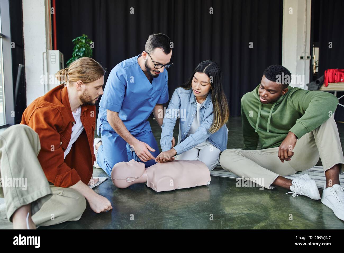 young asian woman practicing life-saving skills by doing chest compressions on CPR manikin near ...