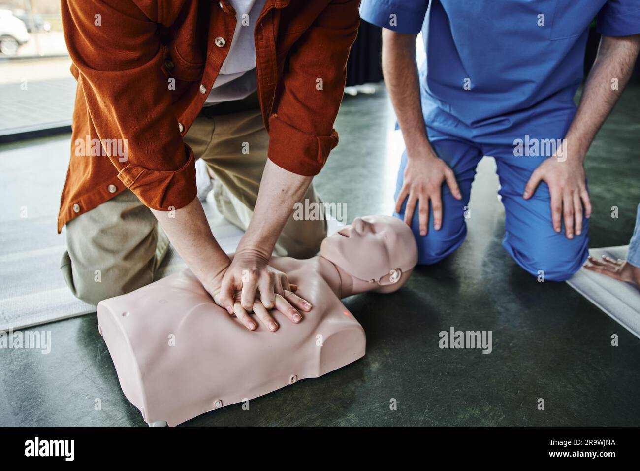 partial view of young man doing chest compressions on CPR manikin ...
