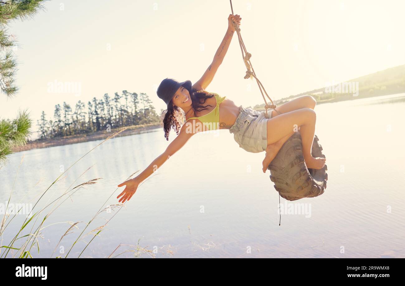 Lake, rope swing and a woman in nature sitting on a tyre for carefree ...