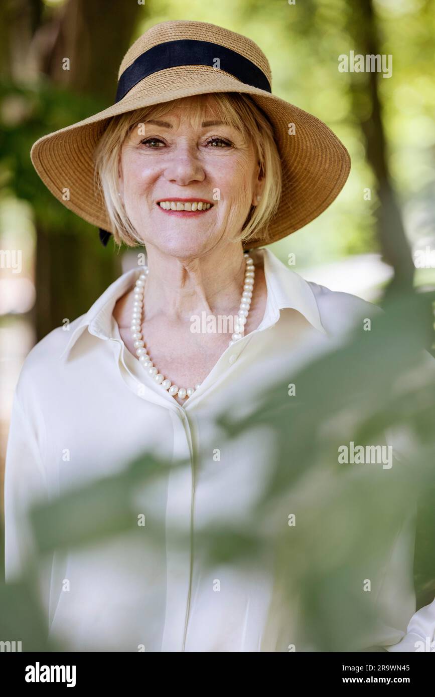 Happy, smiling, older, summery dressed woman with straw hat and pearl ...