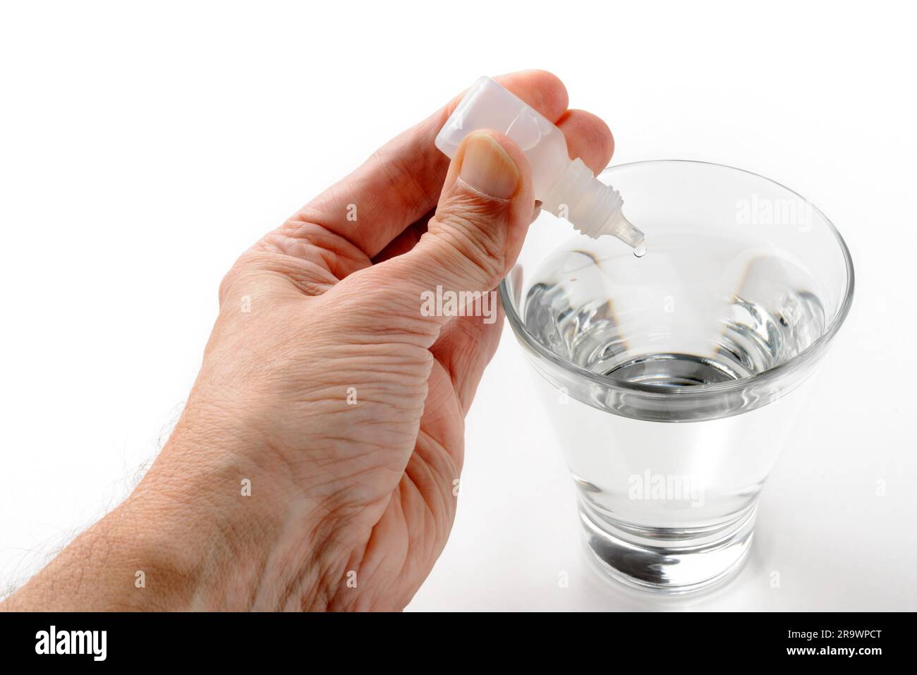 Man's hand putting drops of pharmacy in a glass of transparent water ...