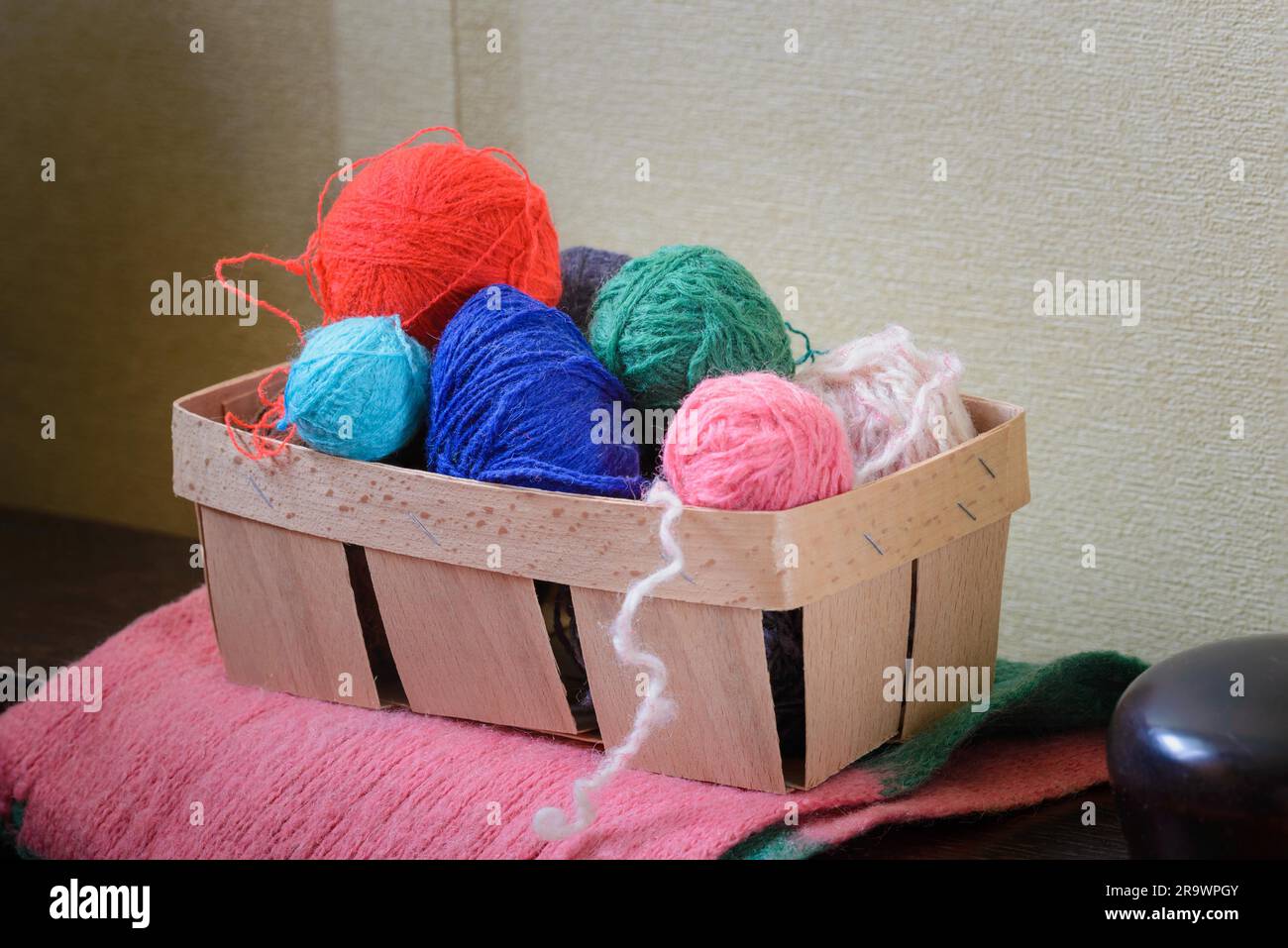 Colorful balls of wool in a crate put on the arm of a wooden armchair ...