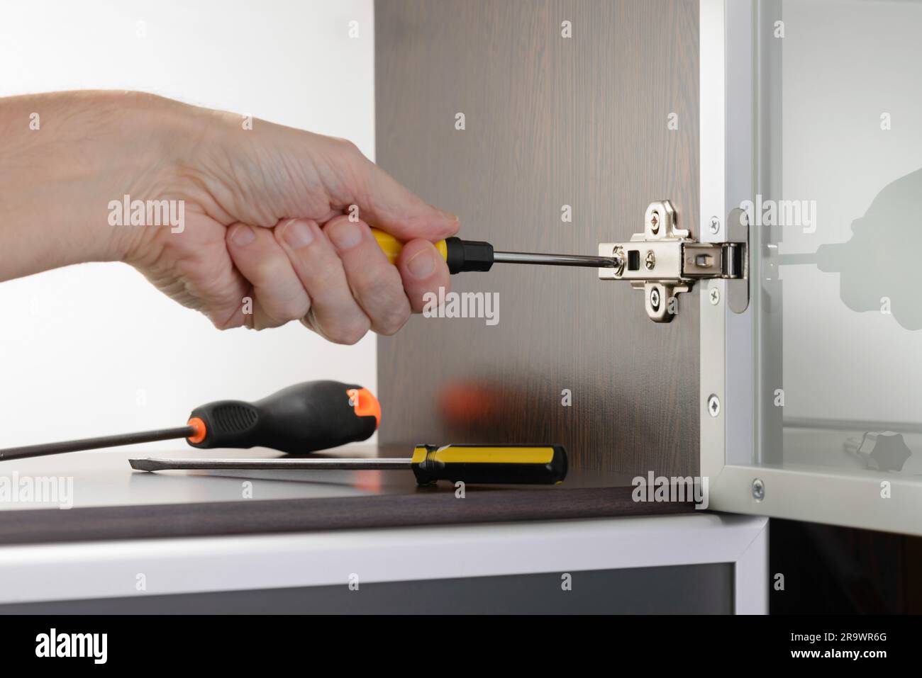 A man uses a screwdriver to adjust a concealed hinge fixed on a modern ...