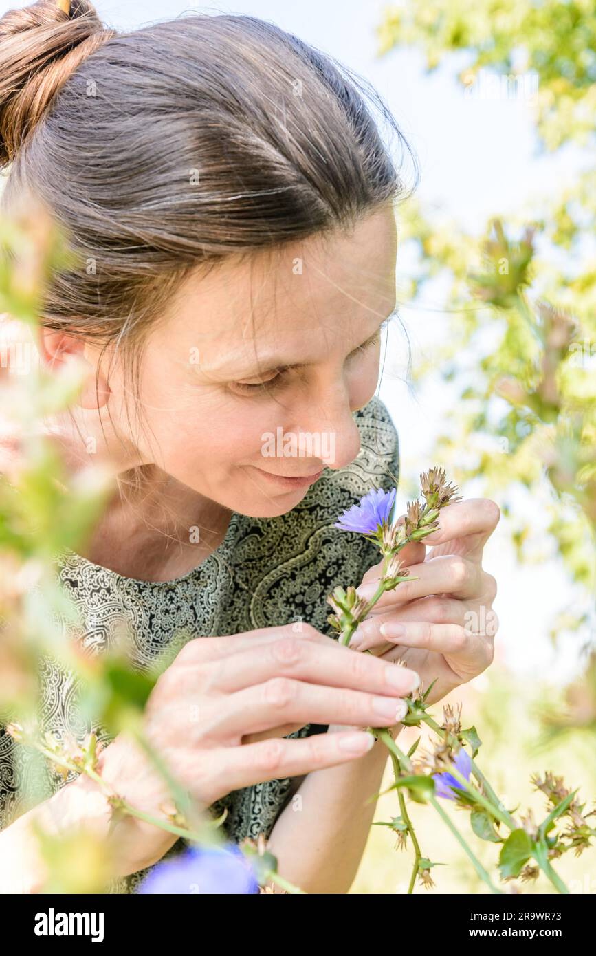A senior woman is sniffing a blue flower in the park during a warm ...