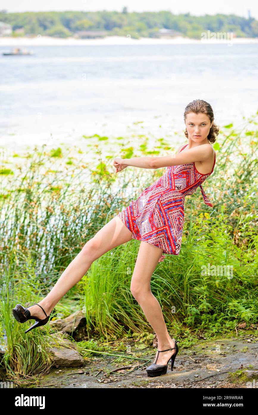 A young woman with a red dress stand close to the river's edge where ...